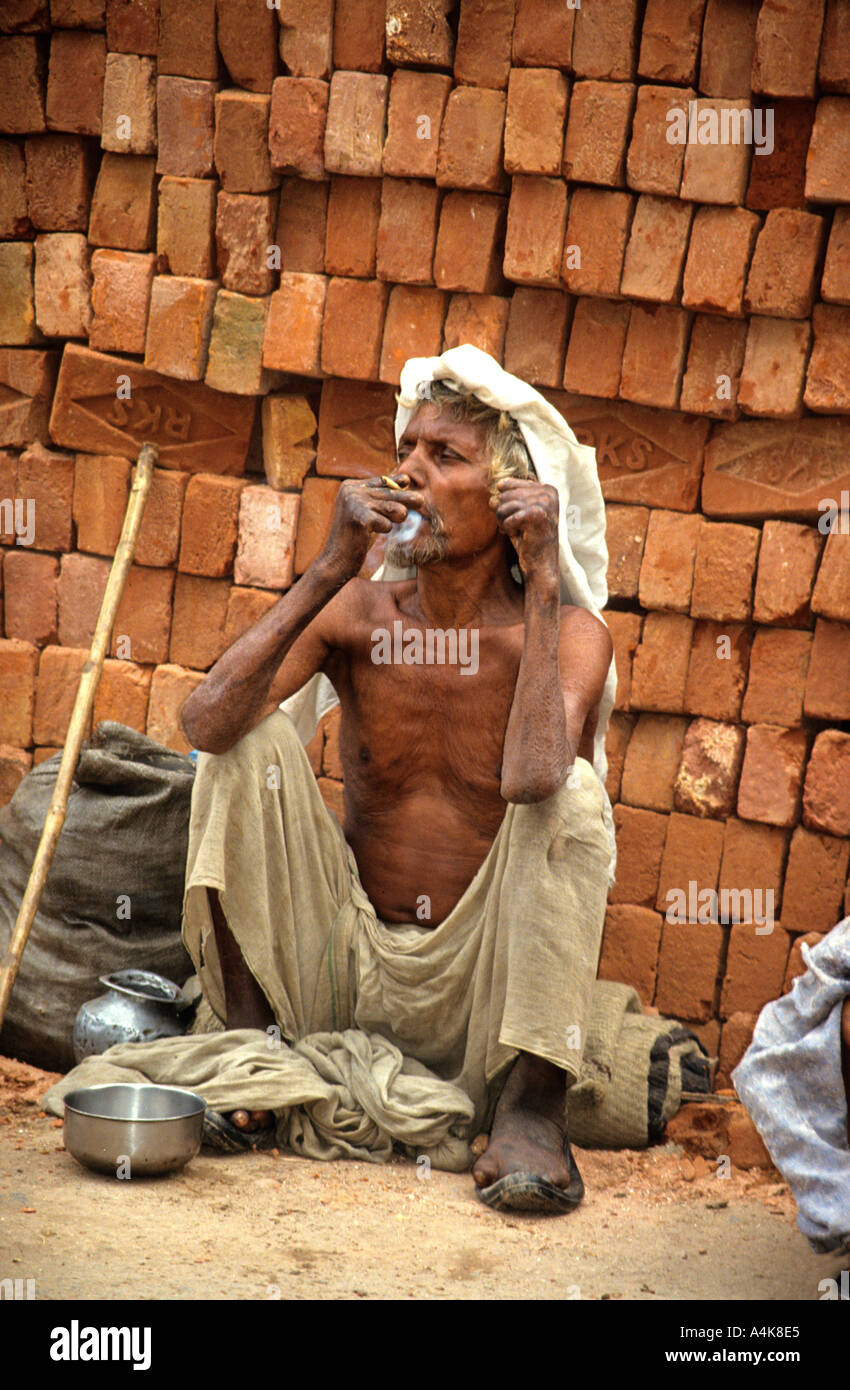 Indian labourer takes a teabreak sitting in front of a pile of bricks ...