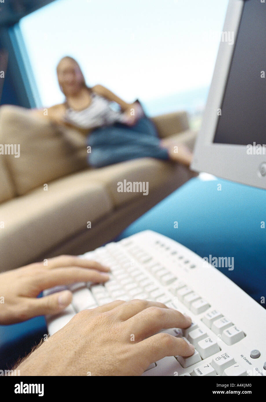 Hands on computer keyboard, woman on sofa in background Stock Photo - Alamy