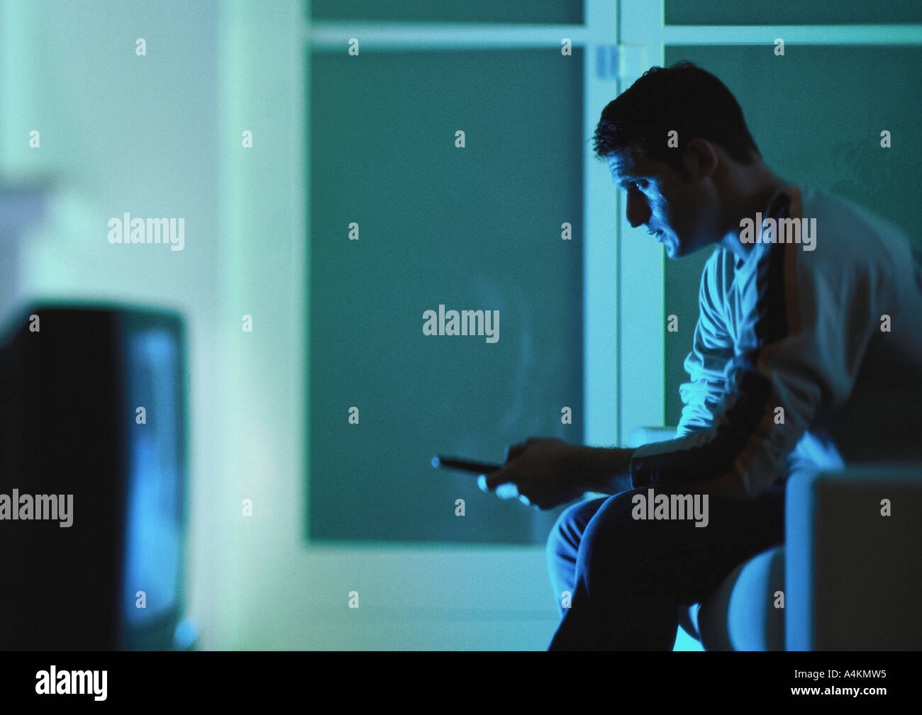 Man sitting on sofa watching television, remote control in hand, side ...