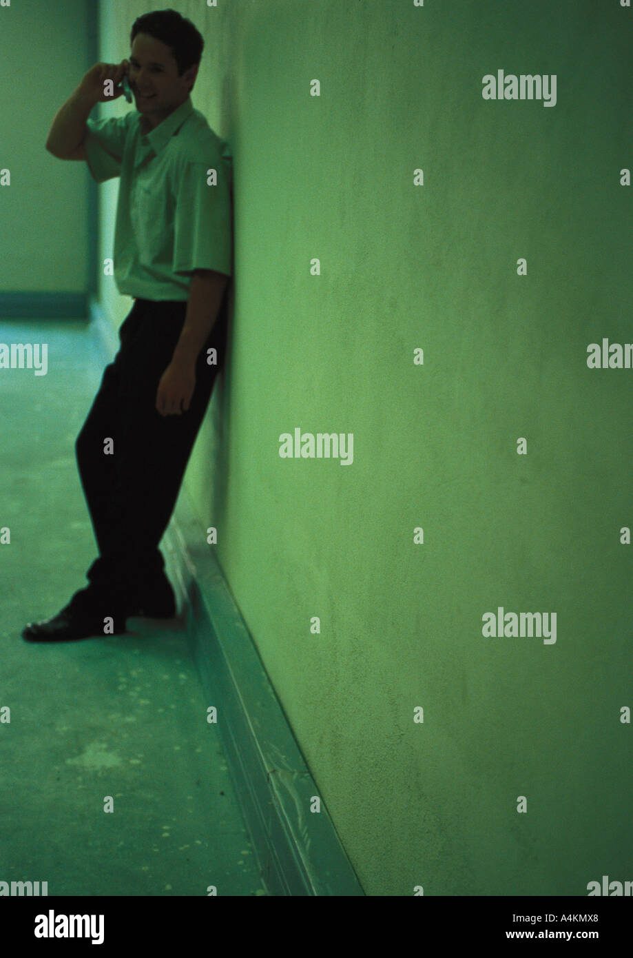 Man using cell phone, leaning against wall Stock Photo - Alamy