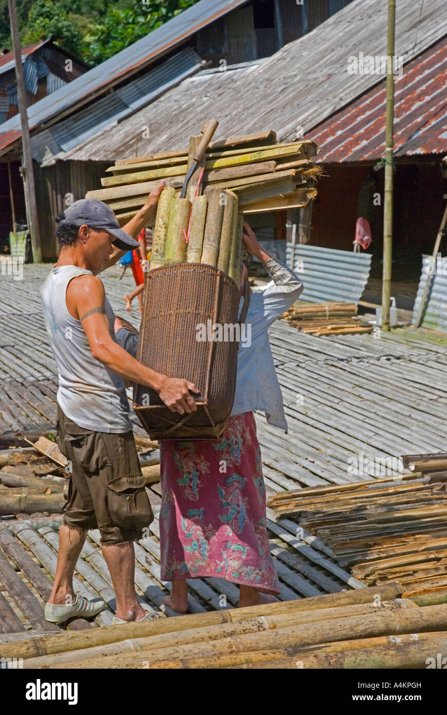A young Bidayuh man helps an old woman lift a large load of bamboo for ...