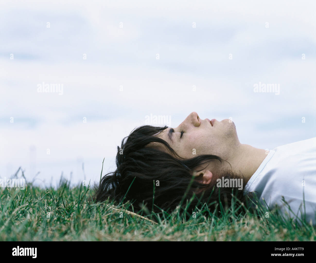 Young man lying on back in grass with eyes closed, head and shoulders ...