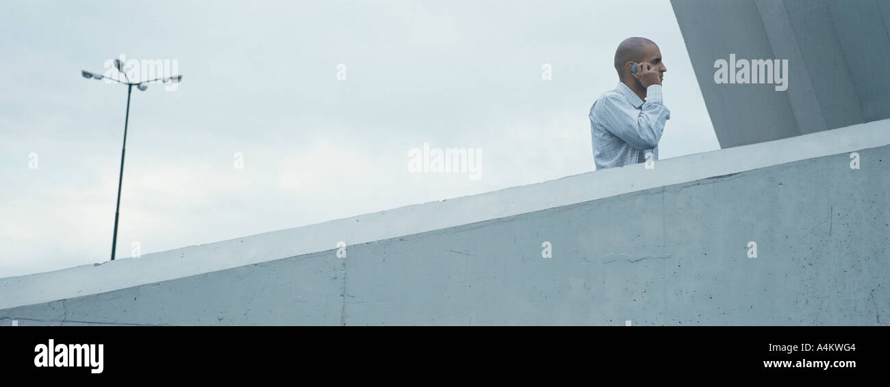 Man standing behind concrete wall talking on cell phone, low angle view ...