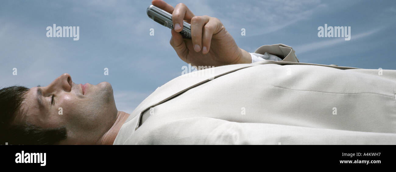 Man lying on back holding cell phone with sky in background, close-up ...