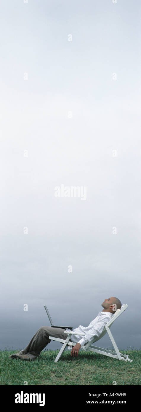 Man sitting in lounge chair with laptop on lap, full length Stock Photo ...