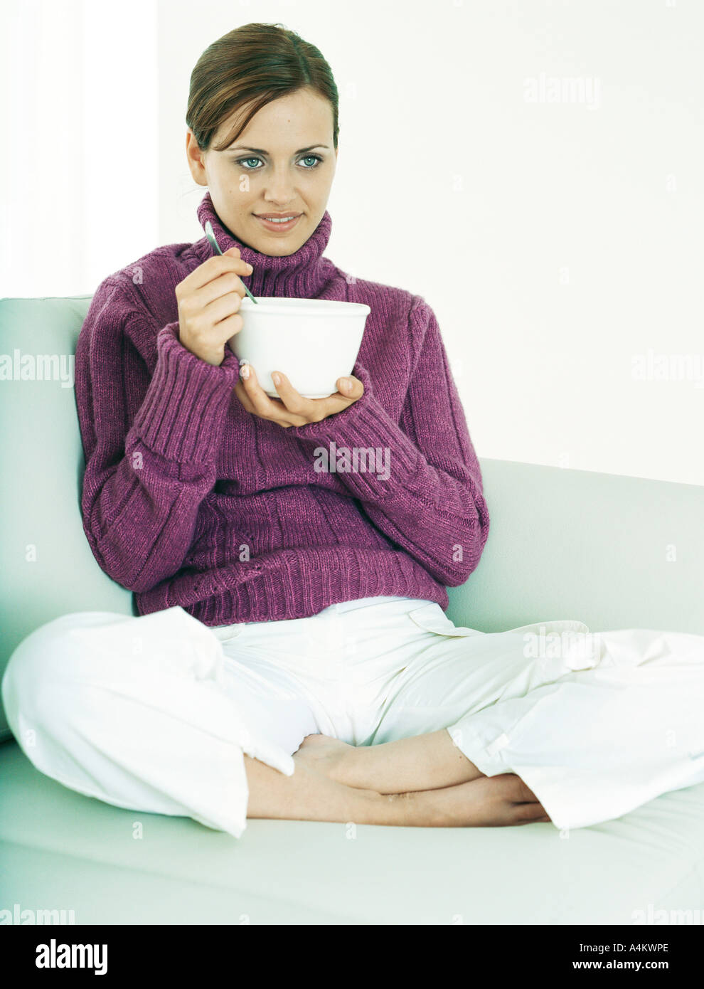Woman sitting indian style on sofa holding bowl and utensil Stock Photo ...