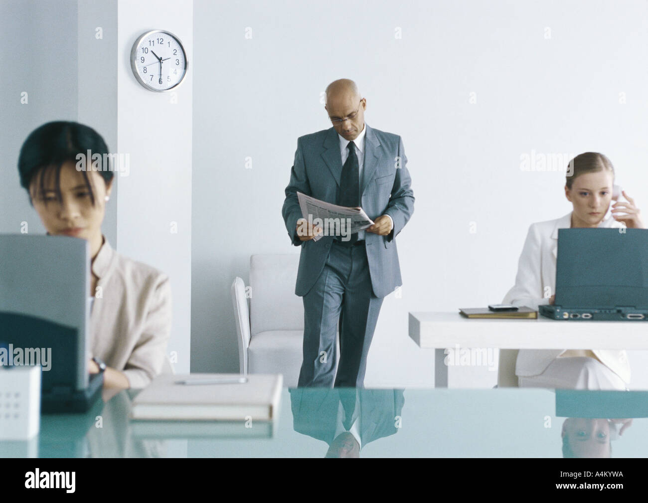 Male executive standing in office reading newspaper, female colleagues ...