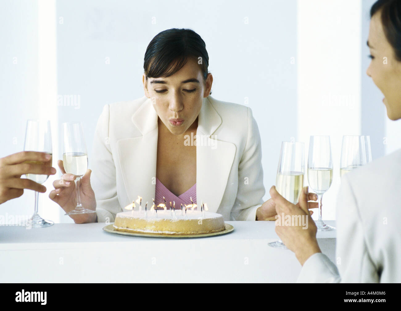 Woman blowing out candles on cake, sitting with other people, holding ...