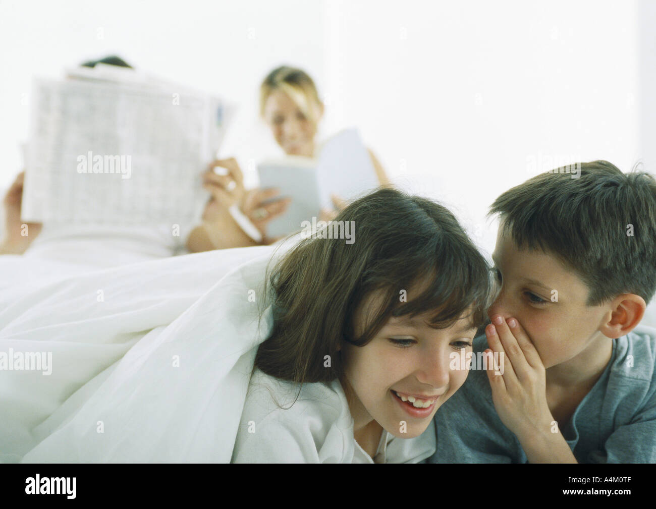 Boy whispering to girl, parents reading in background Stock Photo - Alamy