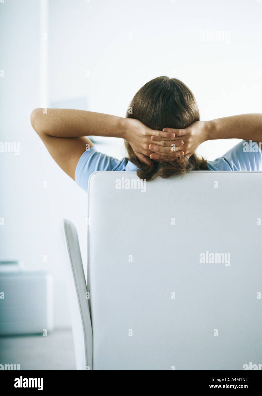 Man sitting on sofa with hands behind head, rear view Stock Photo - Alamy