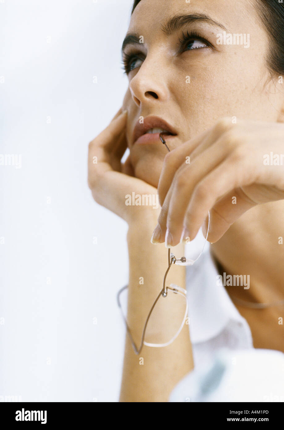Woman holding head and biting on glasses Stock Photo - Alamy