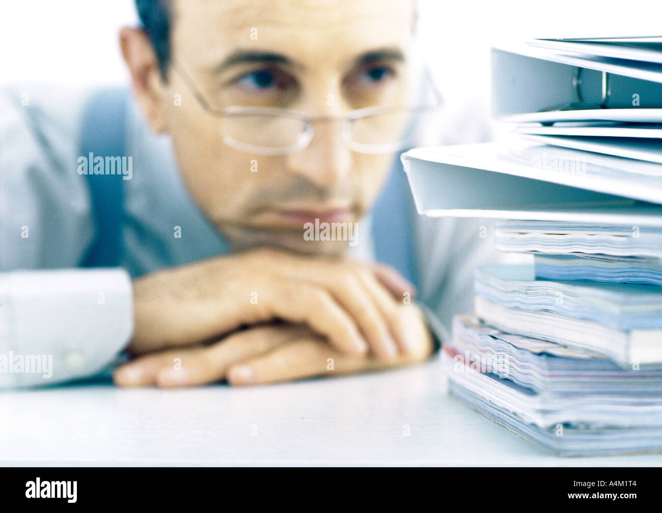 Man resting head on hands, looking at stack of files Stock Photo - Alamy