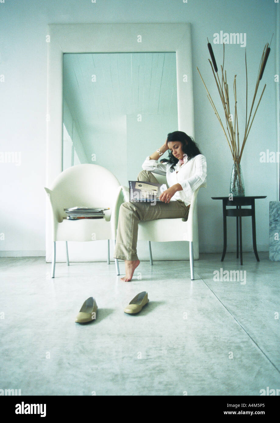 Woman sitting sideways in chair, looking through magazines Stock Photo ...