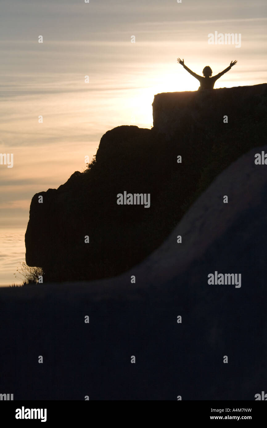 A solitary figure with arms raised, in silhouette against the setting ...