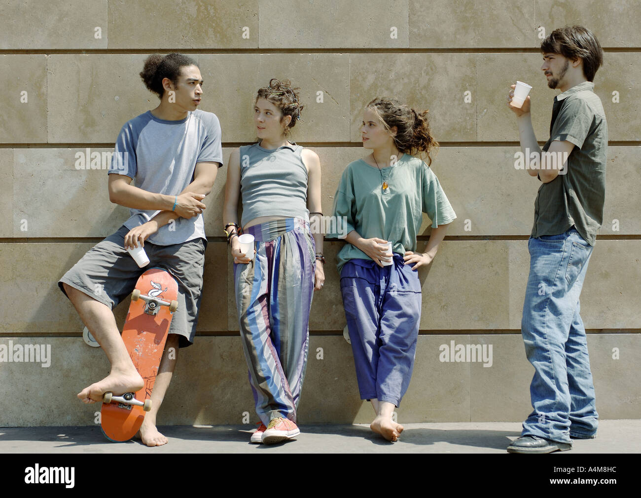Four young friends standing, leaning against wall Stock Photo - Alamy