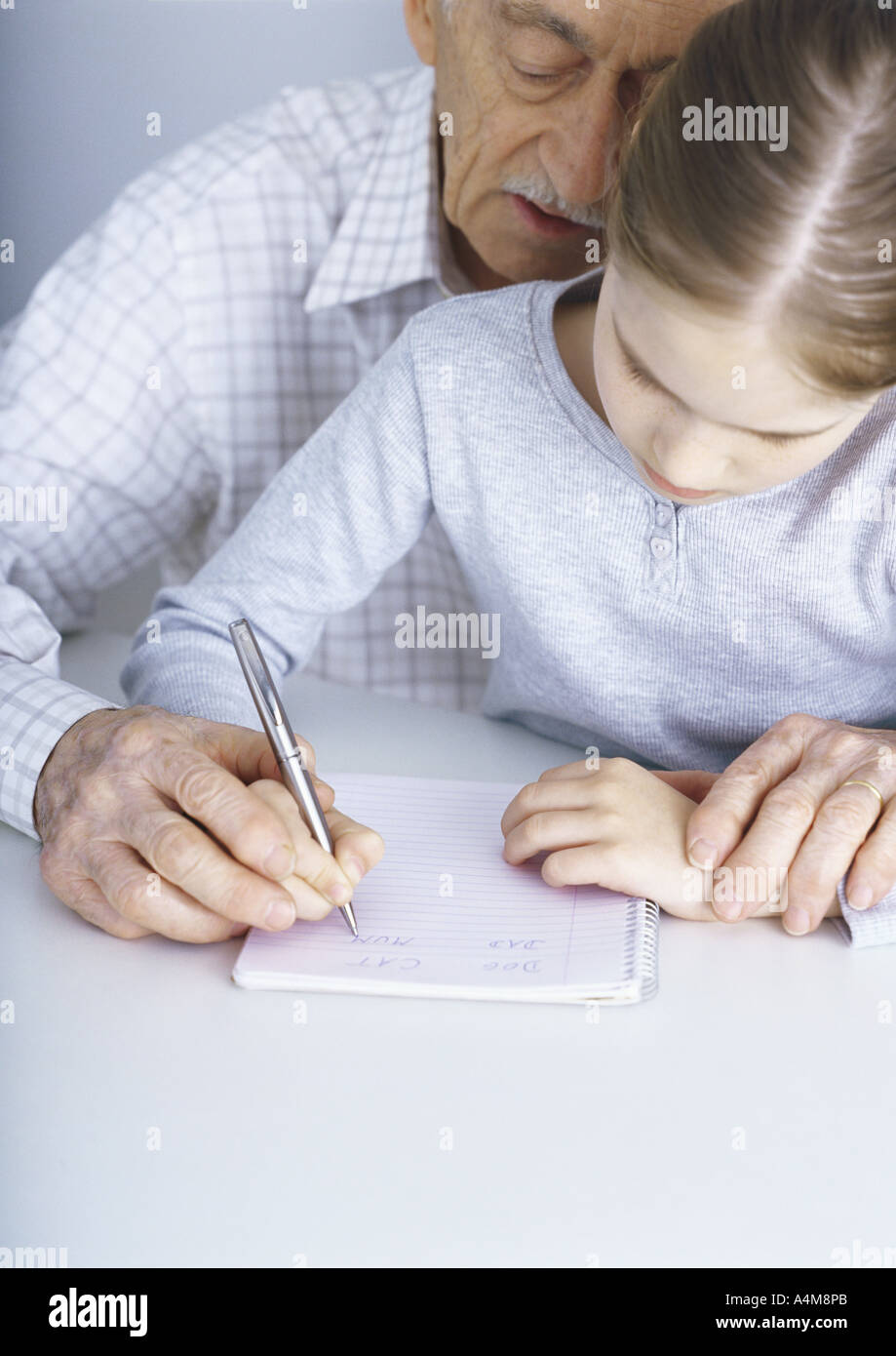 Grandfather helping granddaughter write in notebook Stock Photo - Alamy