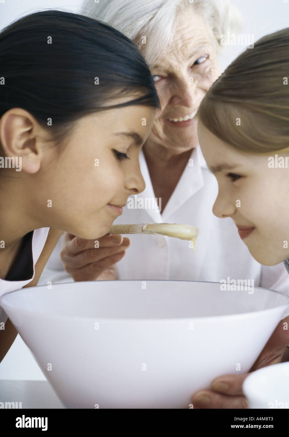 Girls leaning over mixing bowl, grandmother smiling in background Stock ...