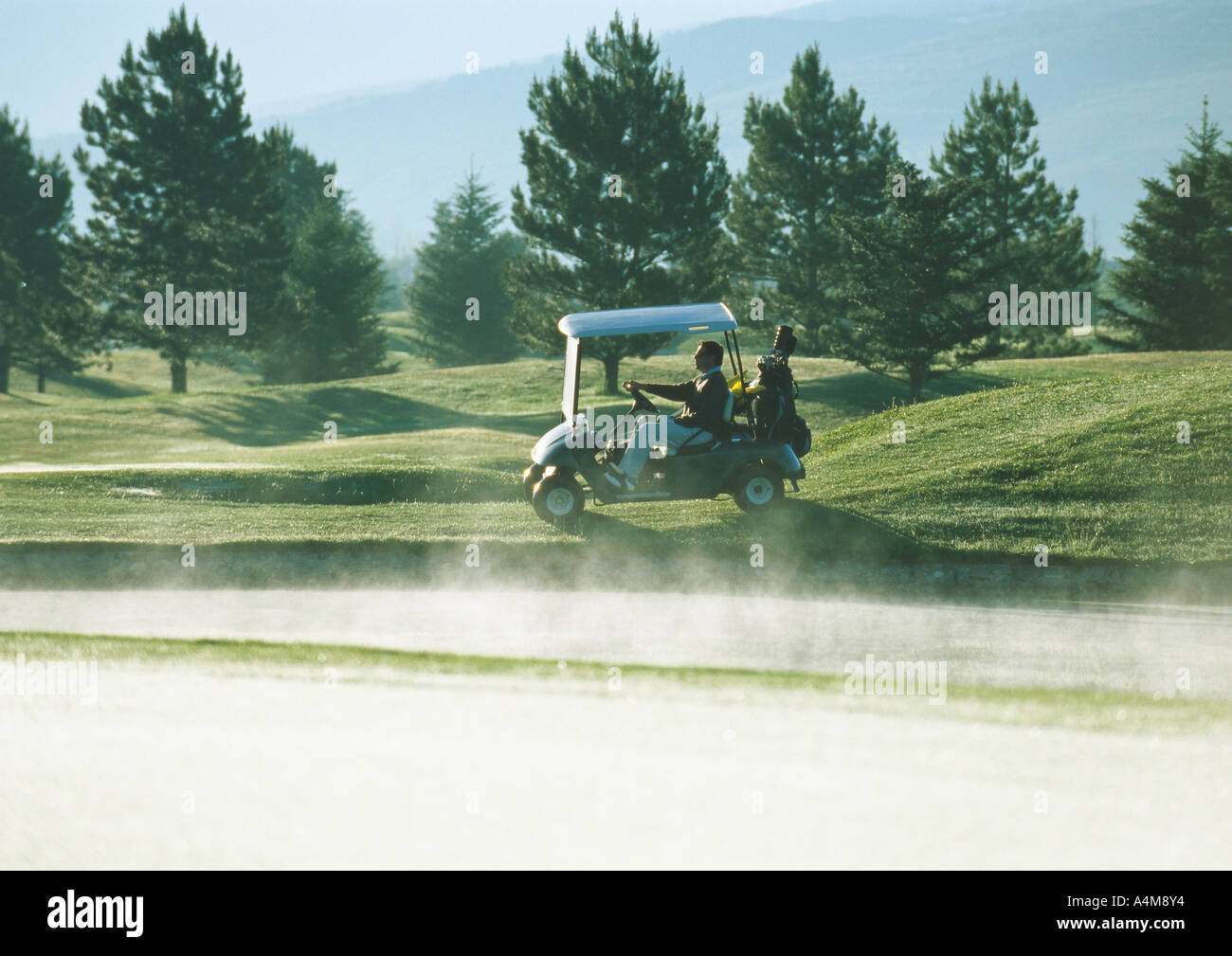 Golfer driving golf cart next to sand trap Stock Photo - Alamy