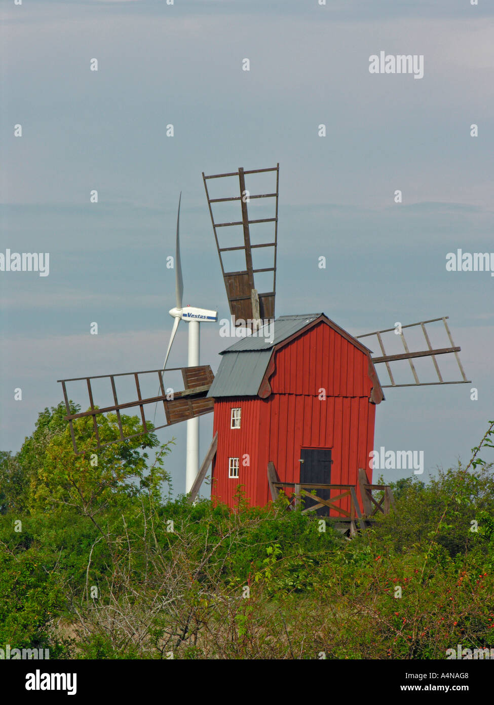 old red wooden windmill with modern wind power station in background ...