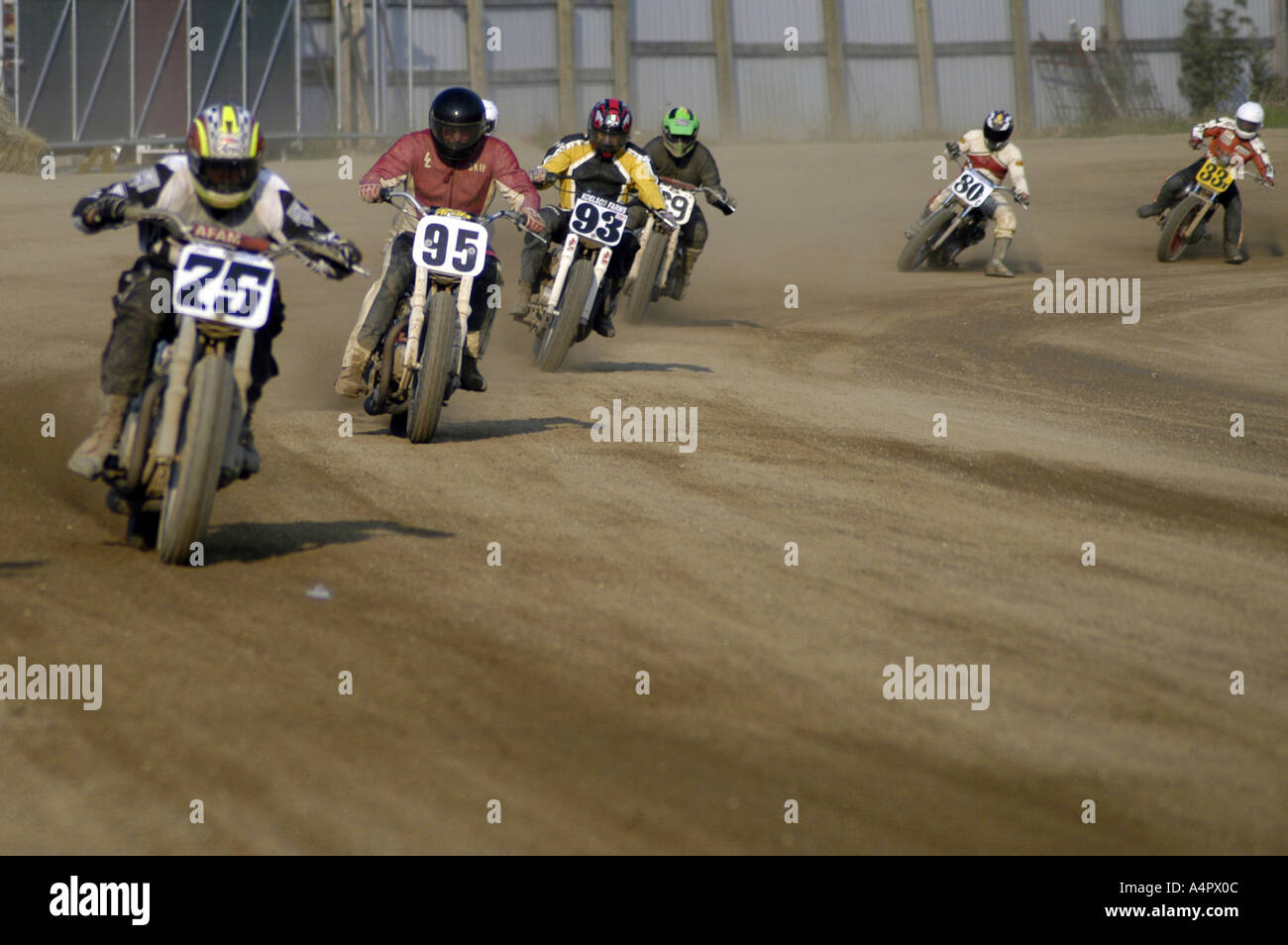 Pack of riders led by 75 vies for position through corner of dirt track ...
