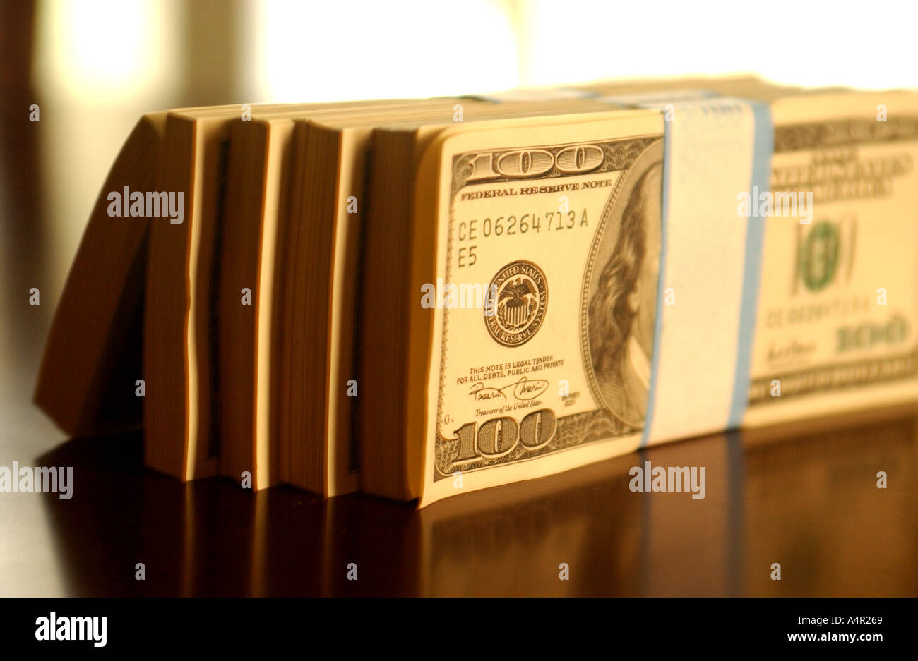 Color image of a banded stack of US currency sitting on a wood table ...