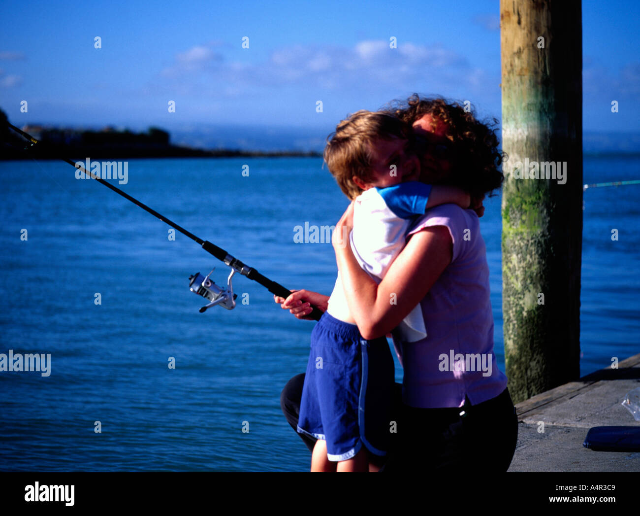 mother and son having a hug whilst fishing of a wharf Stock Photo - Alamy