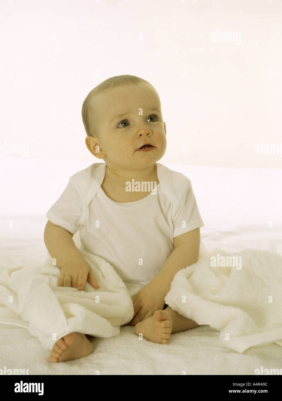 Happy baby boy sitting upright looking up at the camera and listening ...