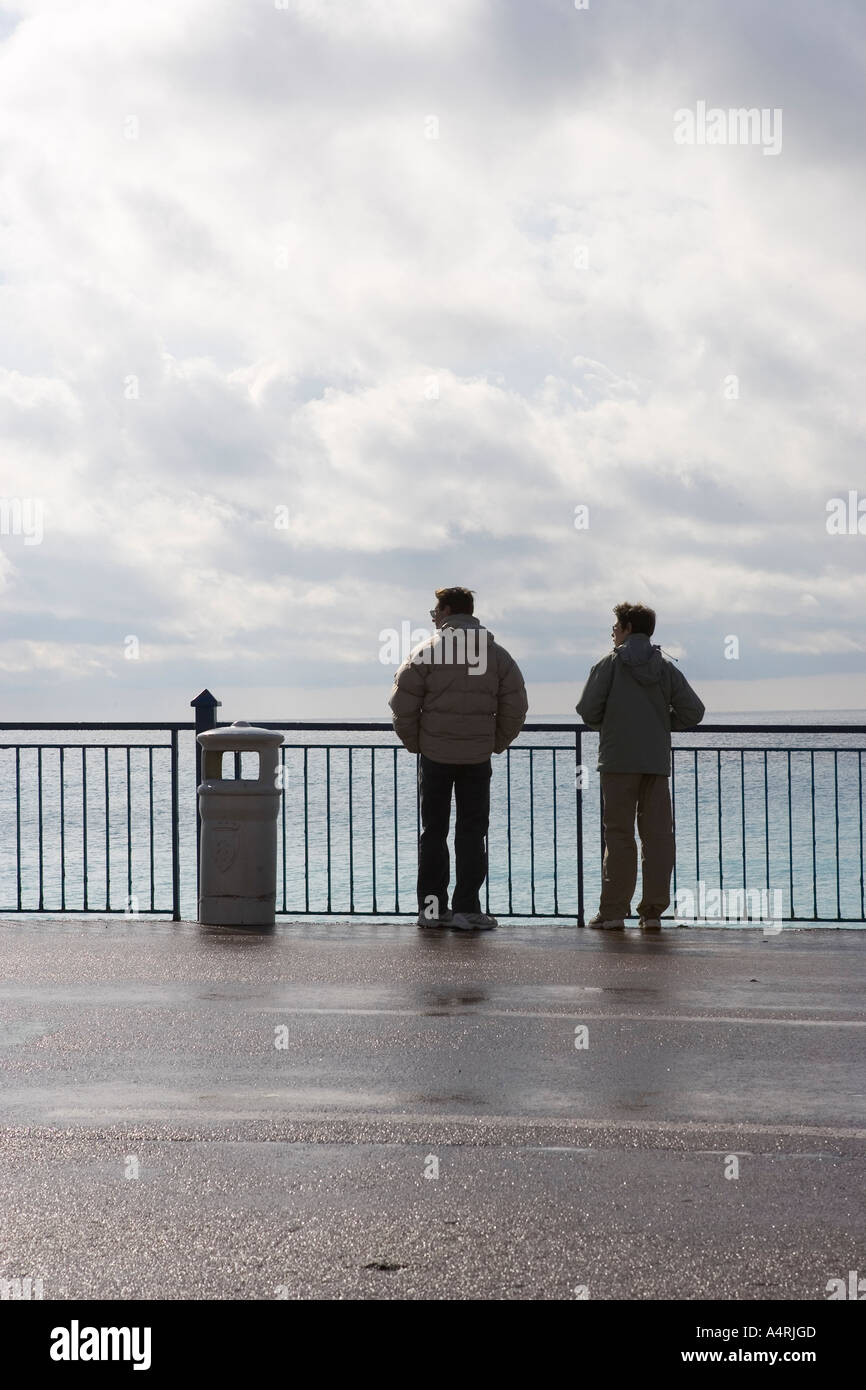 Rear view of two people standing against a railing Stock Photo - Alamy