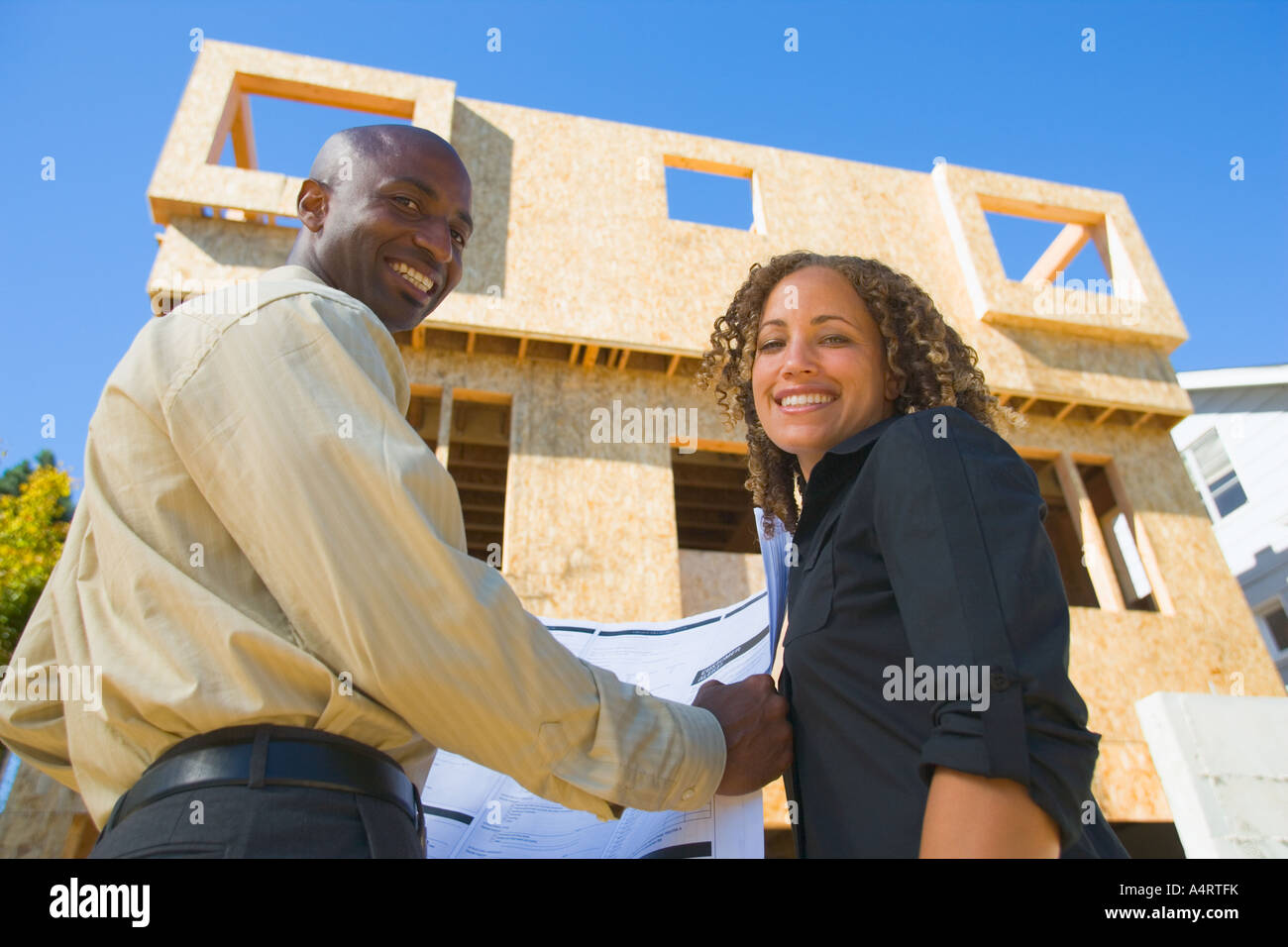 Portrait of smiling young couple with new home under construction ...
