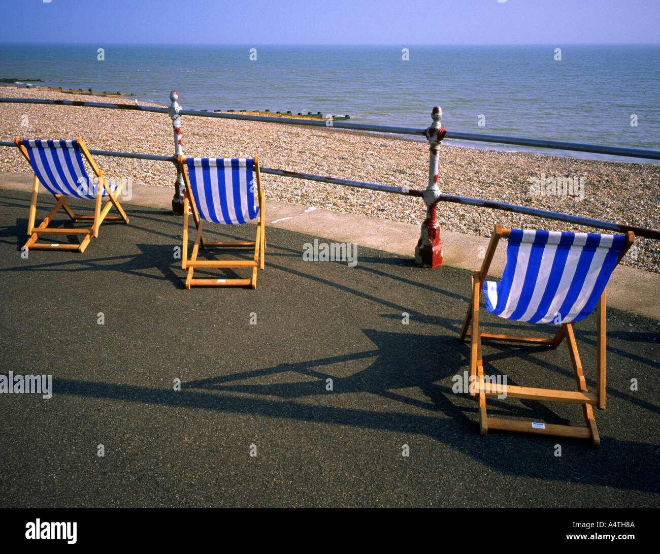Deckchairs lined up on a beach promenade with the sea visible behind ...