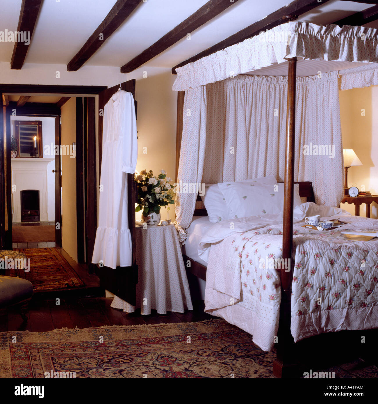 Four-poster bed with floral-sprigged quilt and white drapes in cottage ...