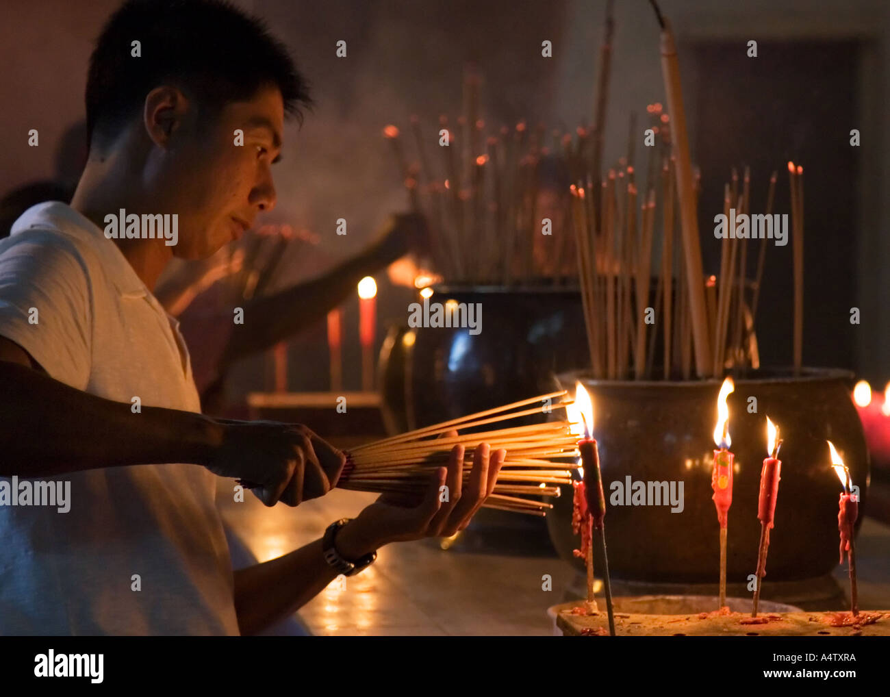A Chinese man lighting incense sticks in a Buddhist shrine in a cave at ...
