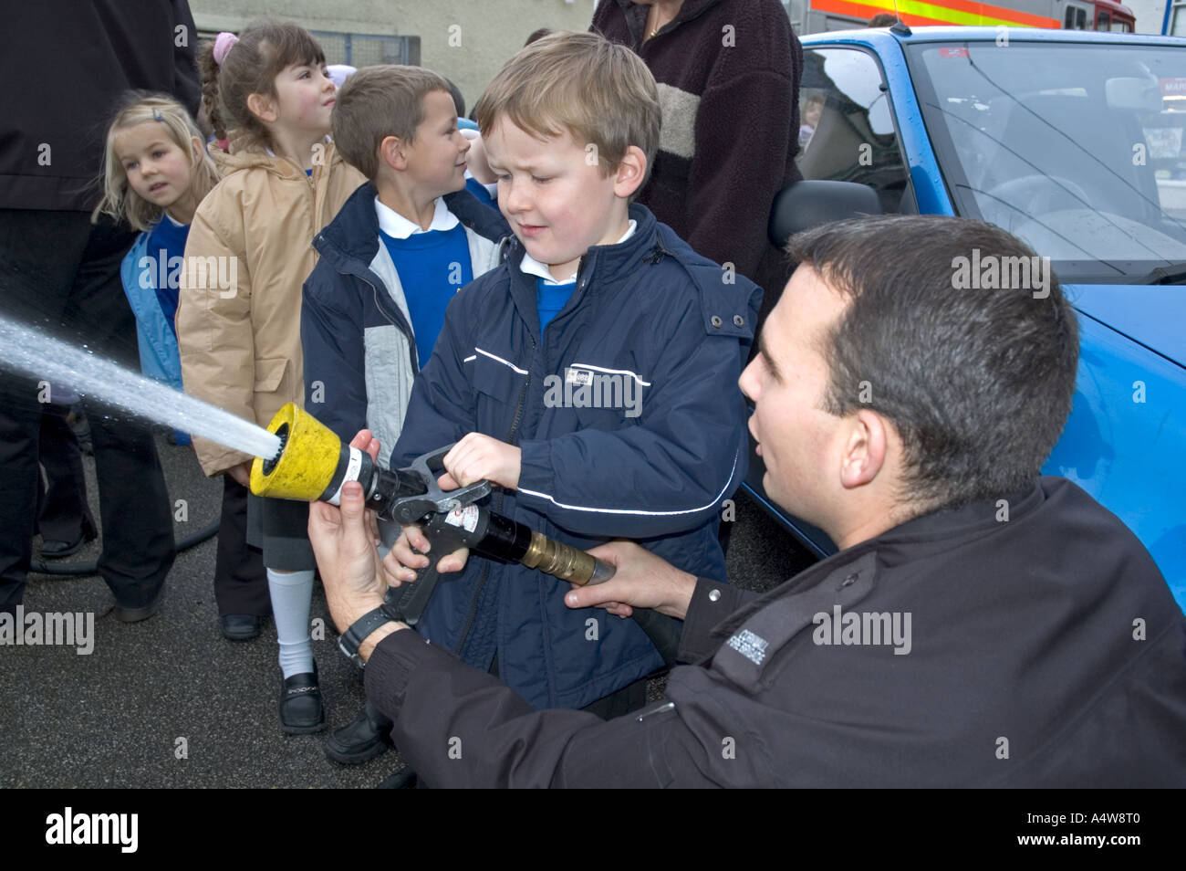 an english firefighter showing primary schoolchildren how to use a hose ...
