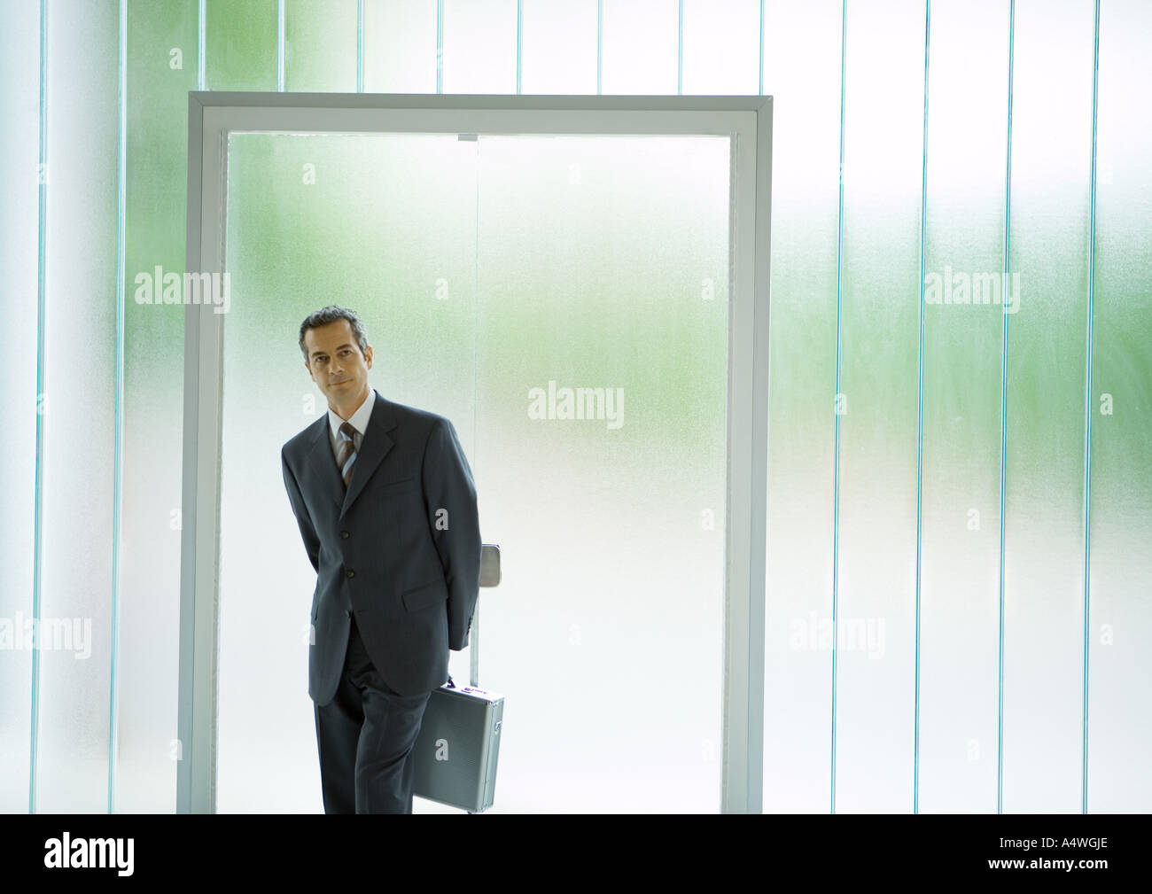Businessman standing in front of door, holding briefcase behind back ...