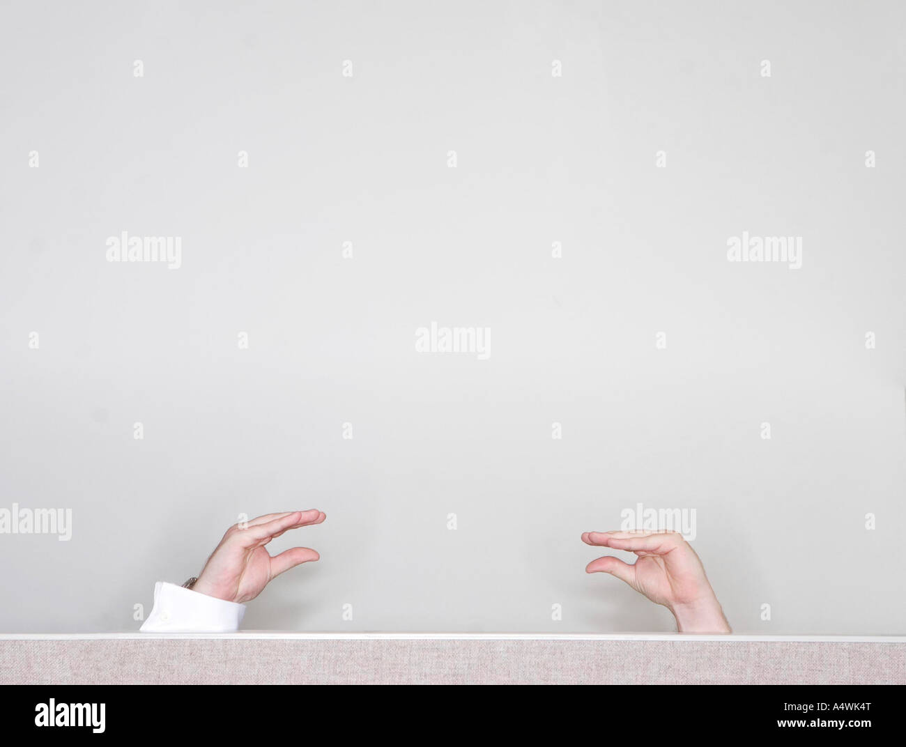 Two hands are talking to each other above a cubical wall with a white ...