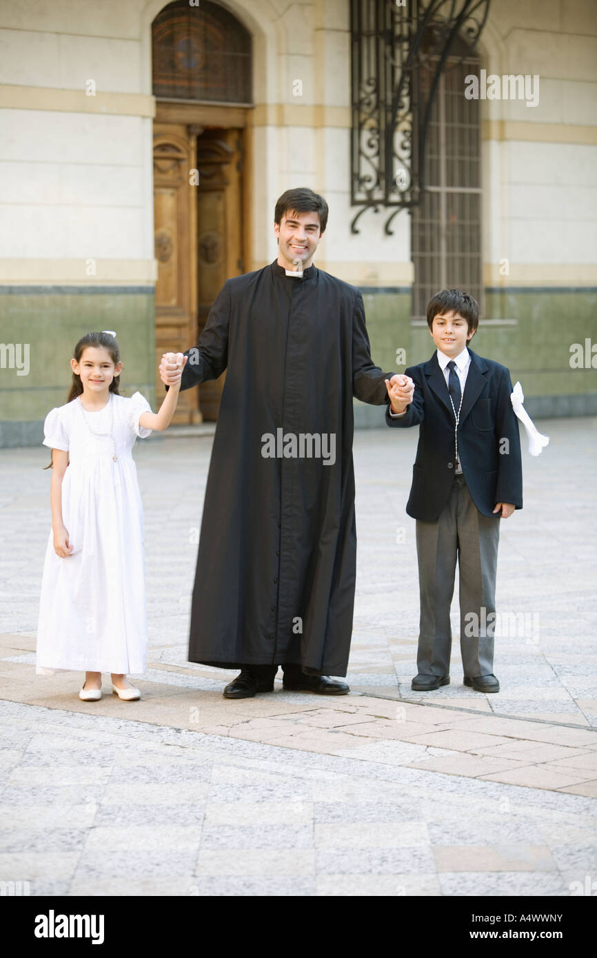 Robed priest holding formally dressed children’s hands Stock Photo - Alamy
