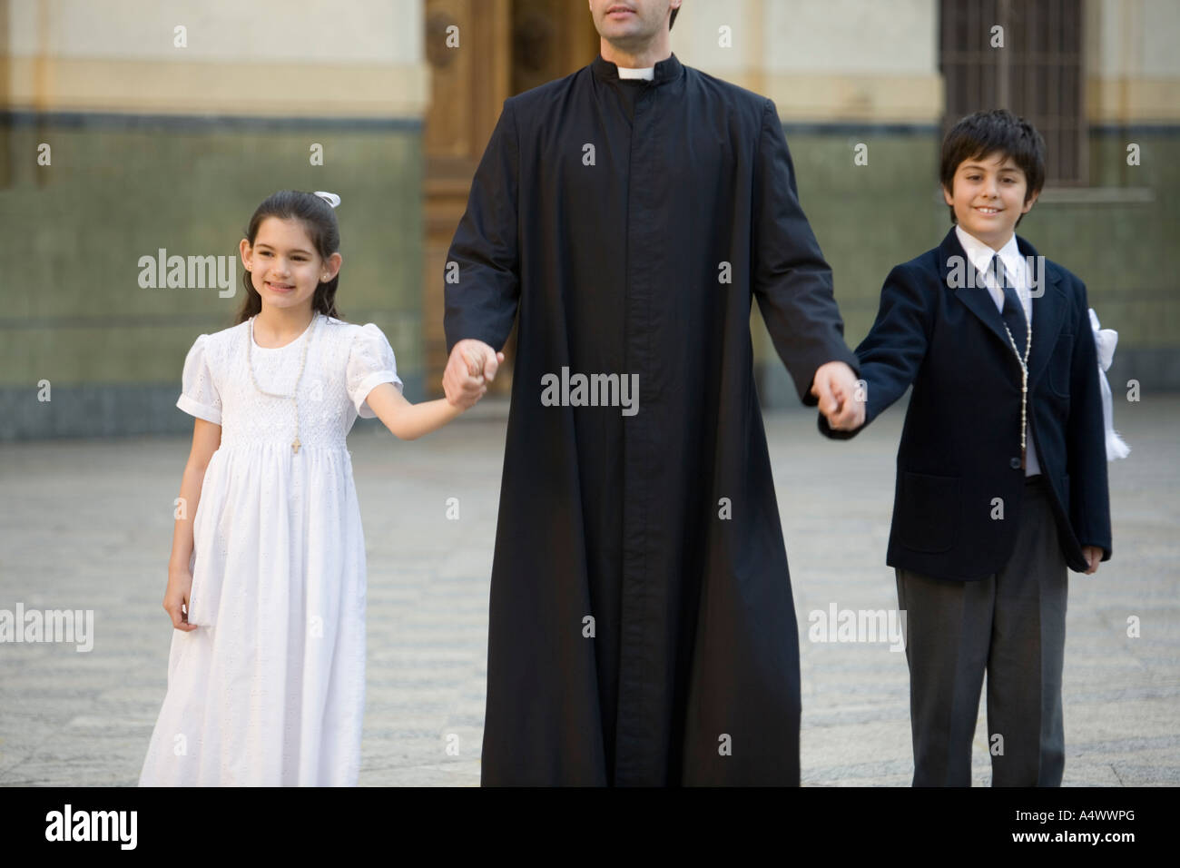 Robed priest holding formally dressed children’s hands Stock Photo - Alamy