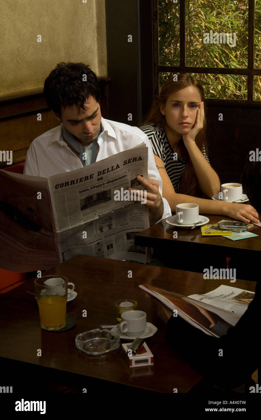 Man reading a newspaper as bored girlfriend sits beside him in cafe ...