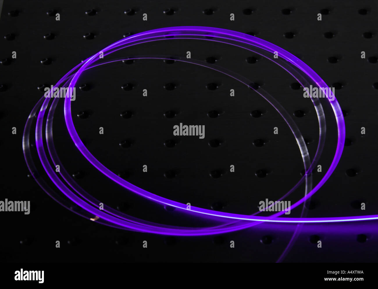 A cladding-pumped doped optical fiber glowing on an optical table Stock ...