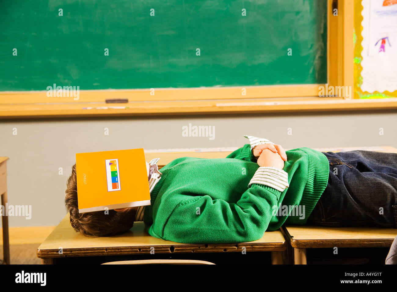 Boy laying on classroom desks with book over face Stock Photo - Alamy