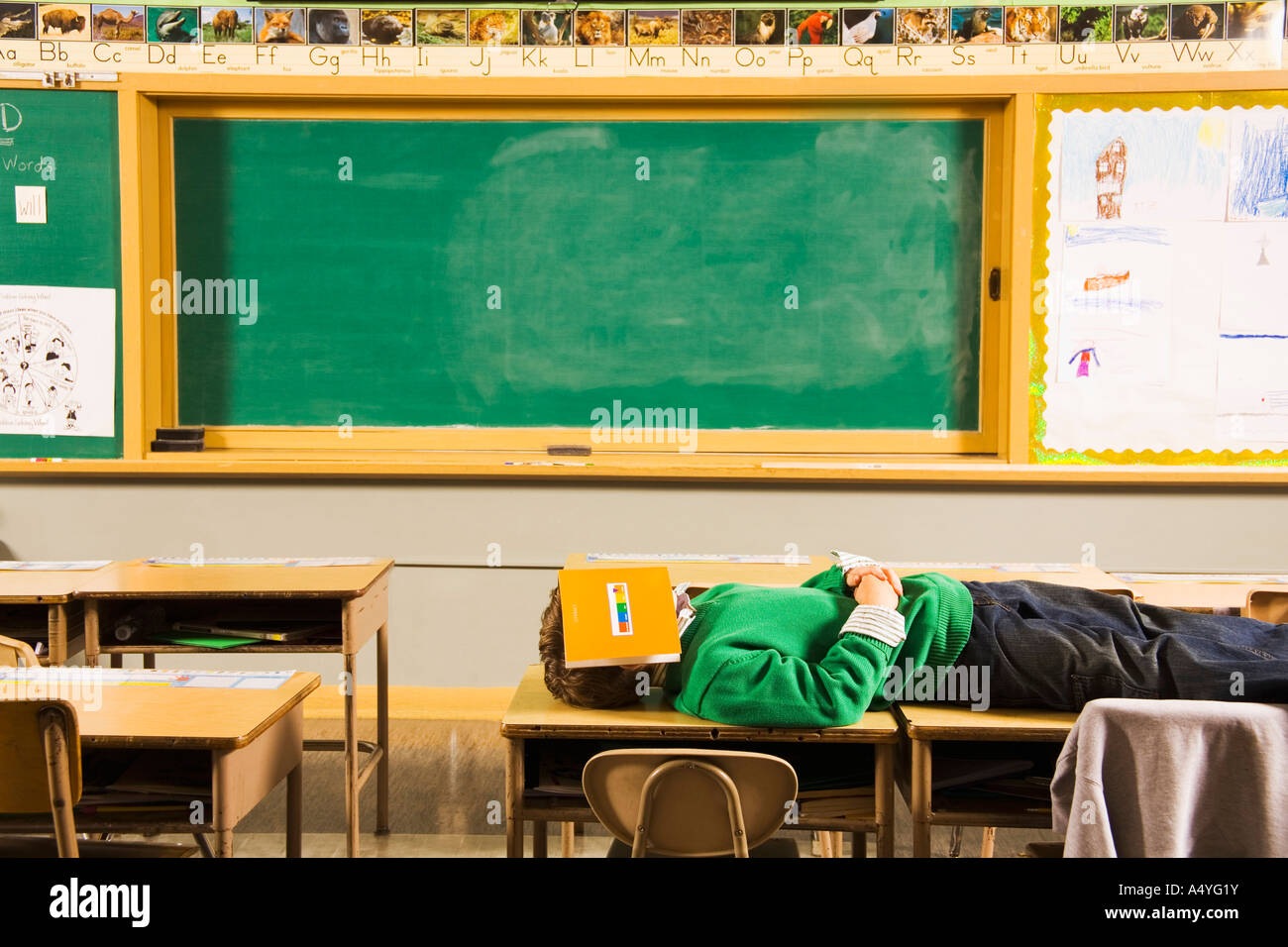 Boy laying on classroom desks with book over face Stock Photo - Alamy