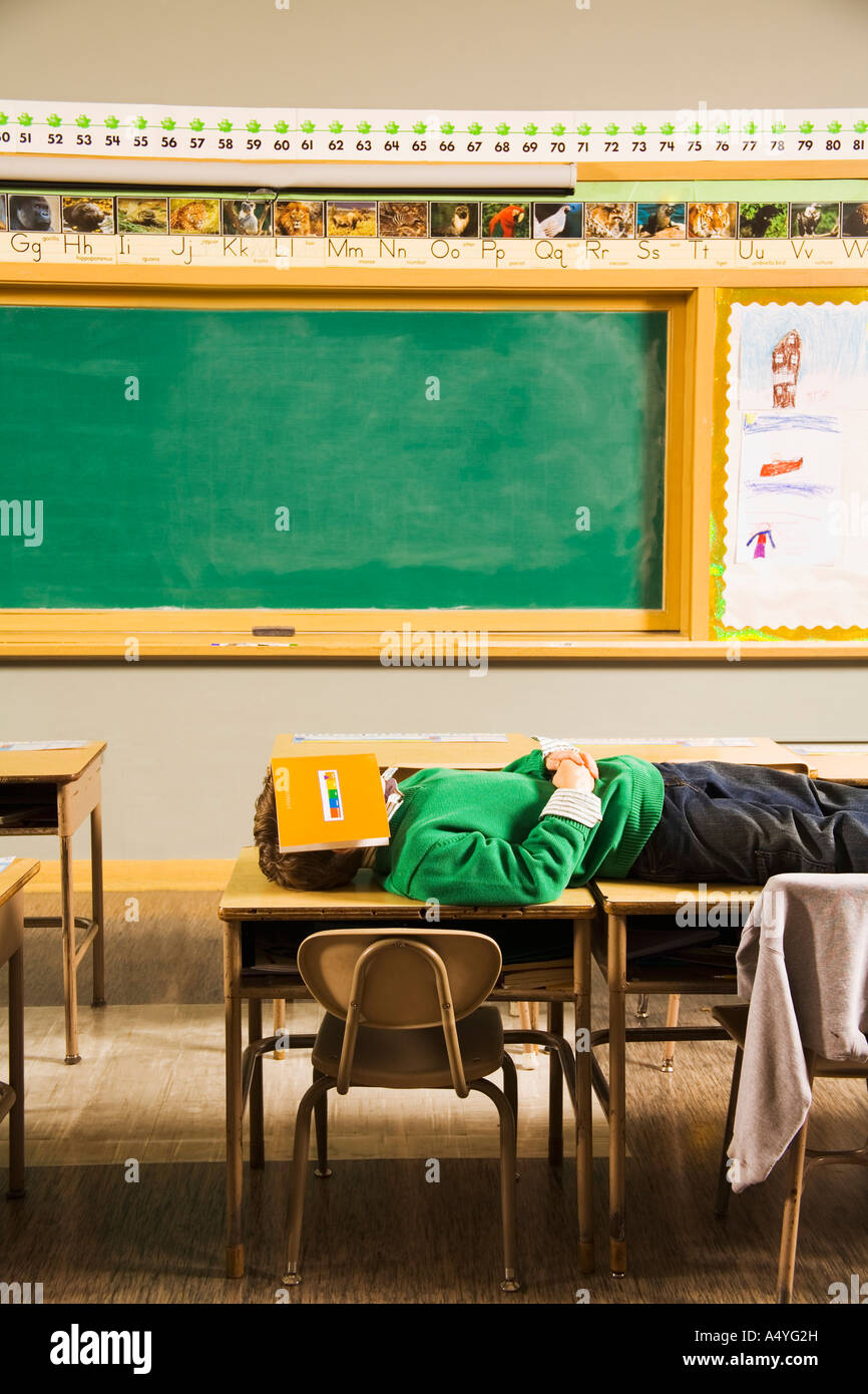 Boy laying on classroom desks with book over face Stock Photo - Alamy
