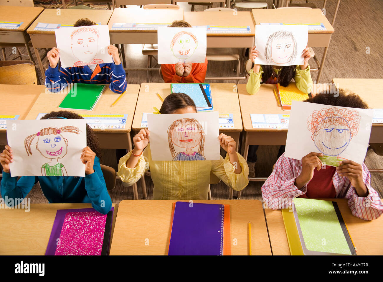 Students holding drawings over faces in classroom Stock Photo - Alamy