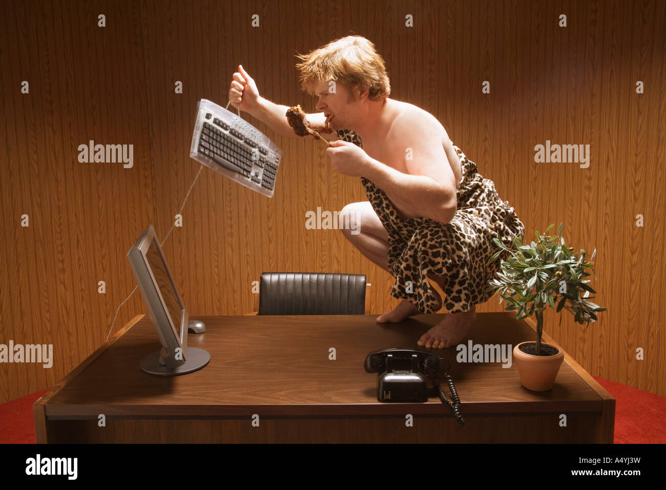 Businessman dressed as caveman crouching on desk Stock Photo - Alamy
