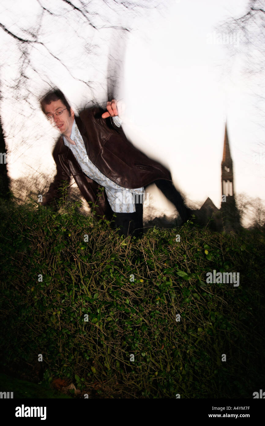 Man jumping over park hedge with leafless branches and church steeple ...