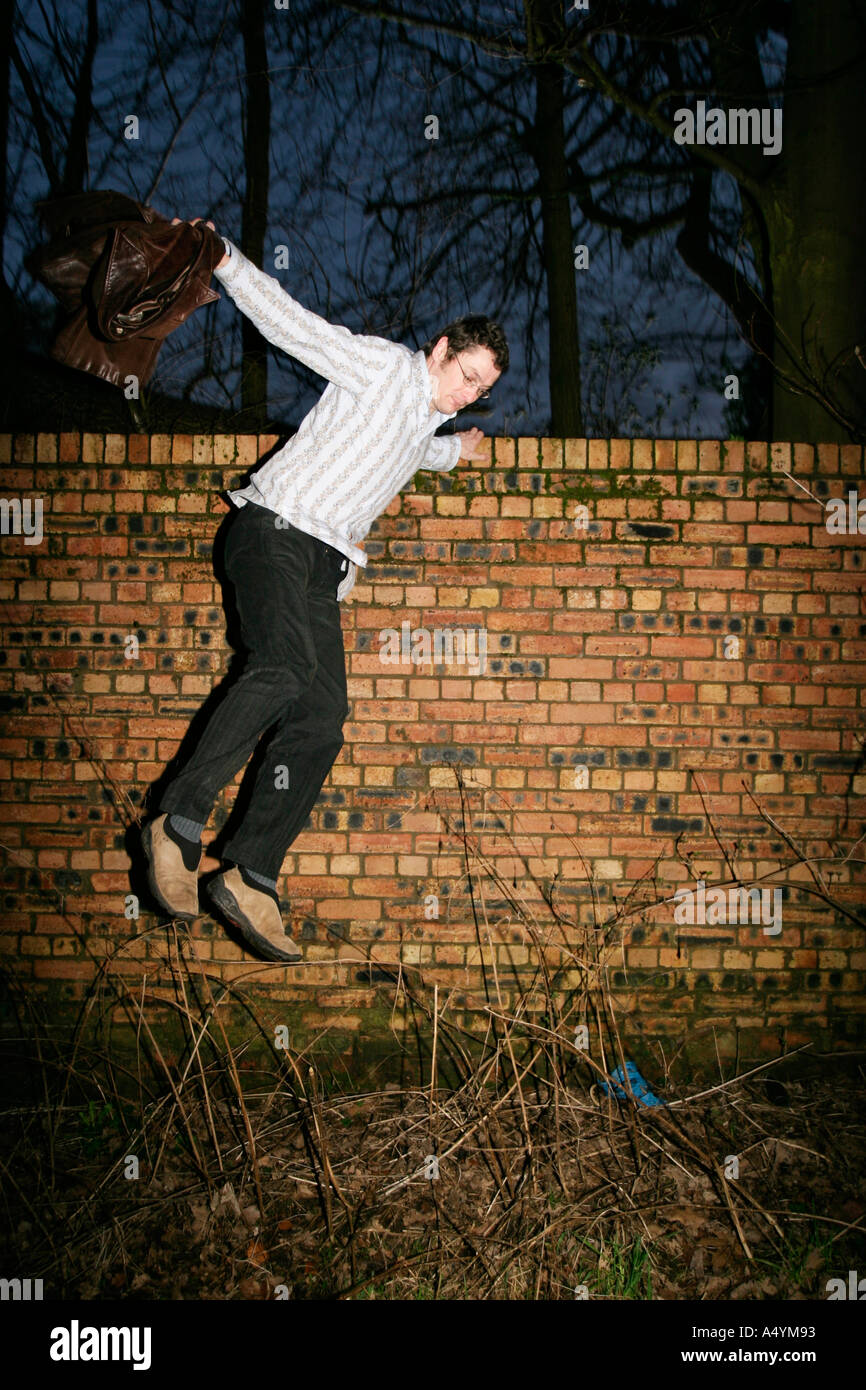 Man leaping from the top of a red bricked wall with leafless trees in ...