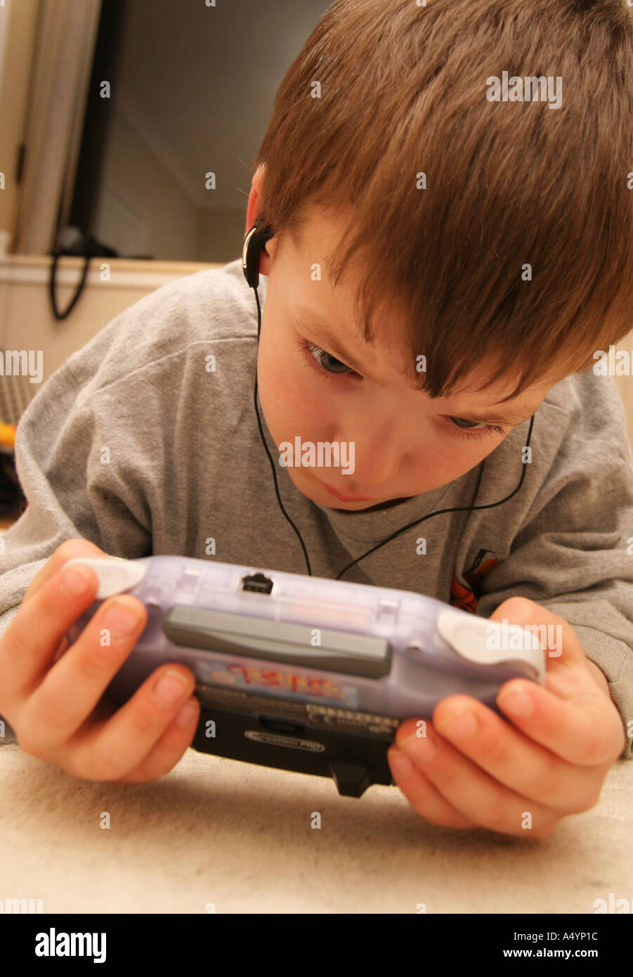 Boy playing game console lying on the living room rug earphones in ears ...