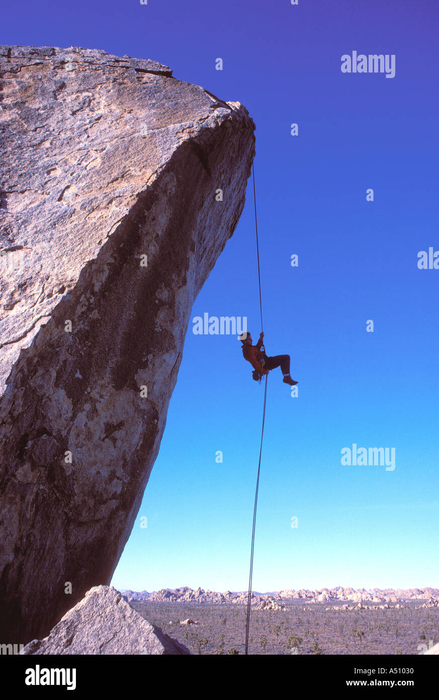 Rock climing man rappeling off of rock with desert landscape in ...