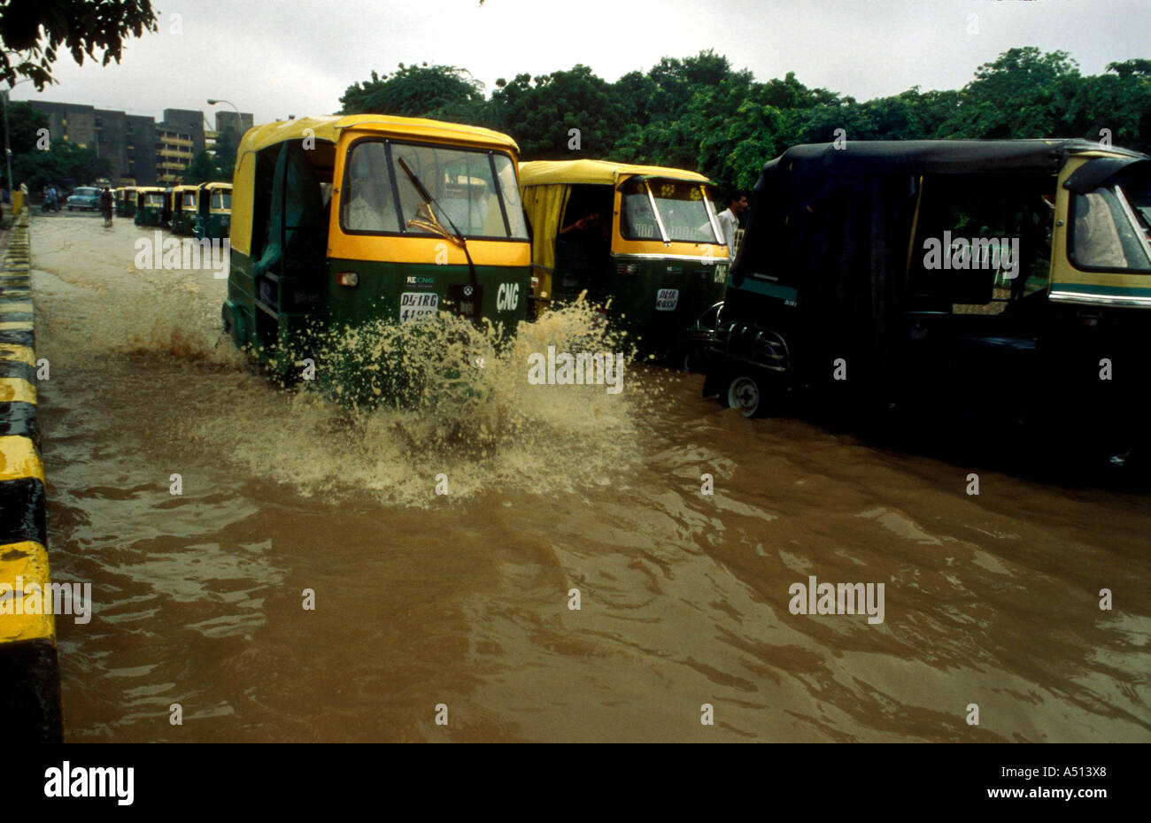 Auto rickshaw passing through a water clogged street besides a CNG ...