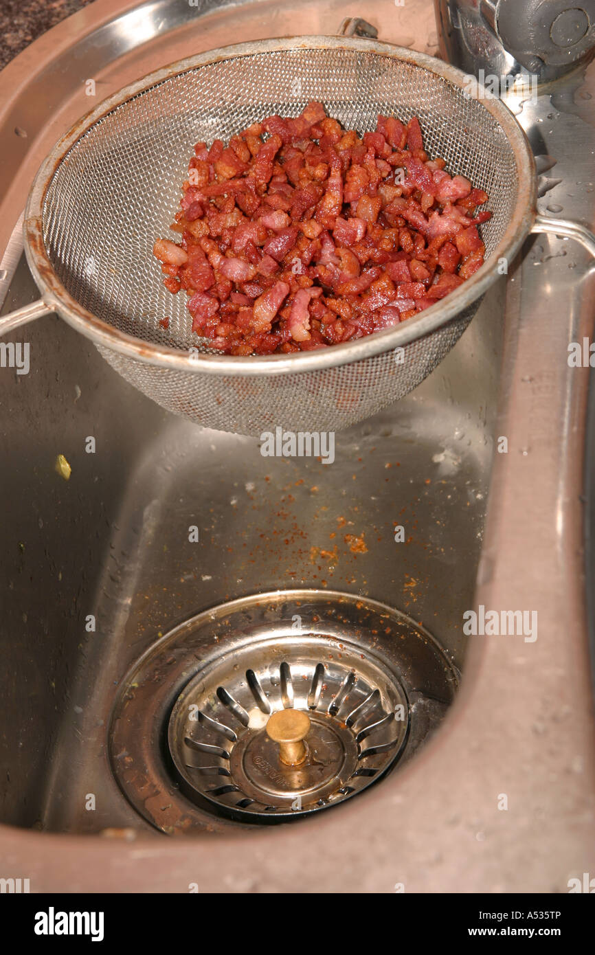 Close up of small pieces of bacon in a sieve. Fat dripping off into the ...